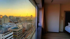Quarto de hotel com uma grande janela e vista para a cidade, uma cama e uma porta.