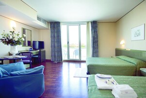 Quarto de hotel com duas camas, uma mesa com cadeira, televisão e vista para o exterior.