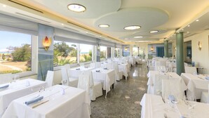 Um restaurante com toalhas de mesa brancas, mesas bem dispostas e grandes janelas com vista para o exterior.