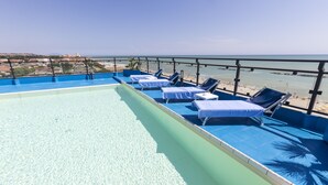 Piscina no terraço com espreguiçadeiras e vista para a praia.