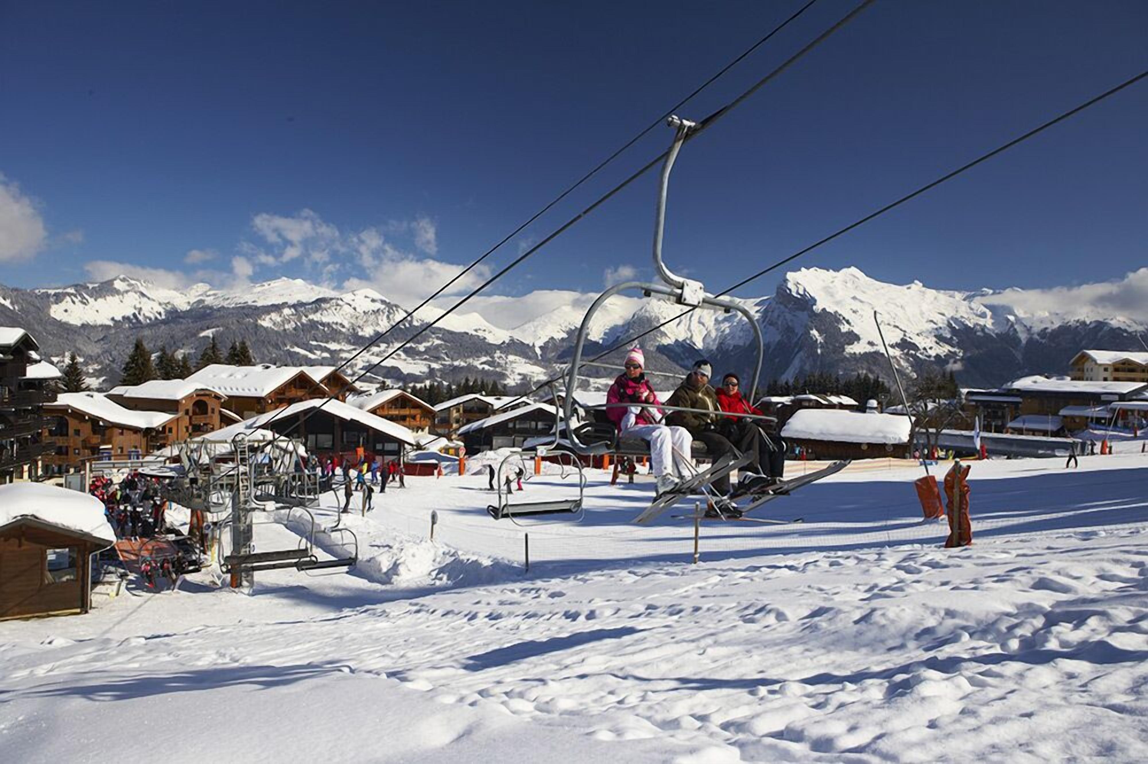 Um teleférico com passageiros, cercado por edifícios cobertos de neve e montanhas ao fundo.