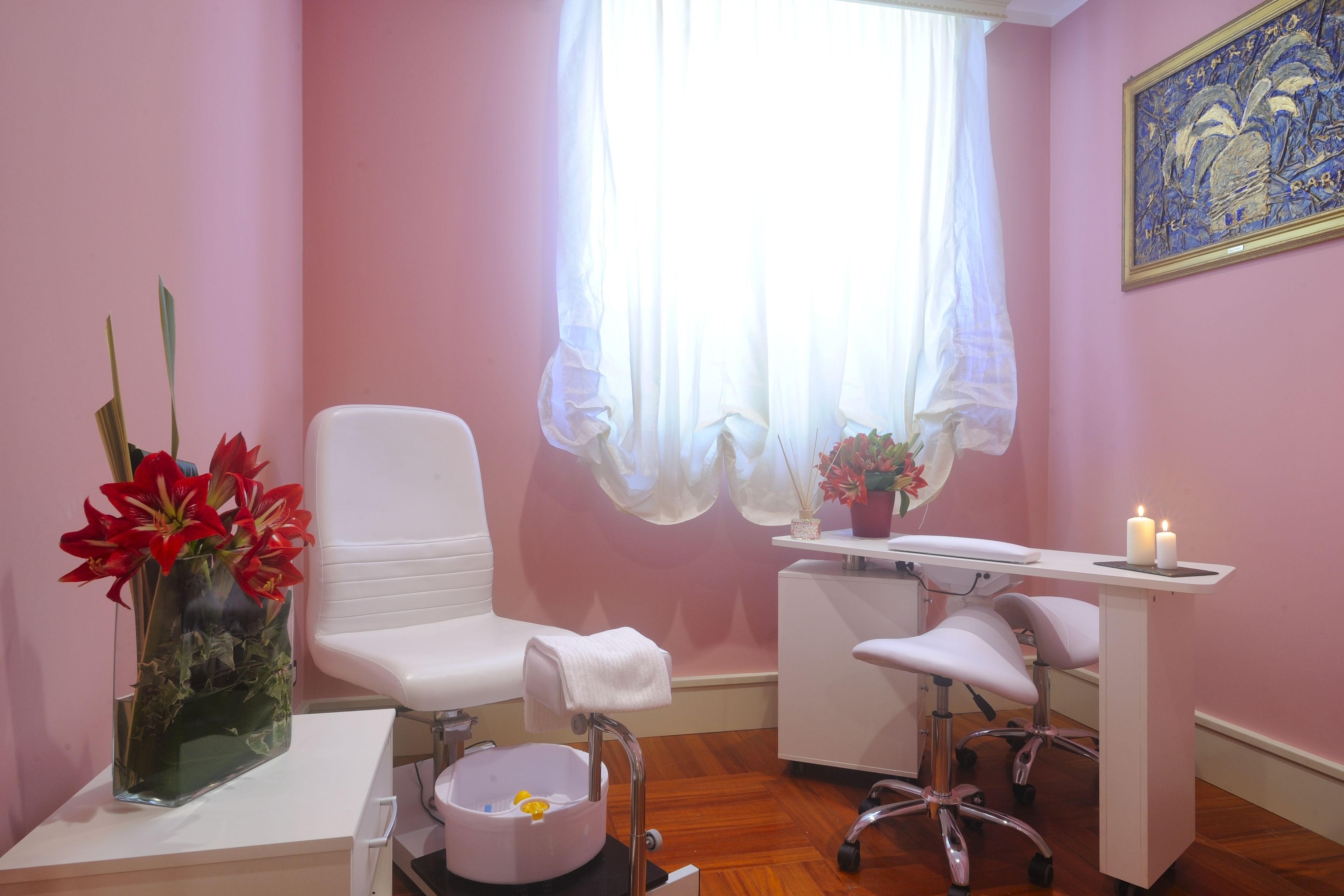 Quarto com decoração em tons de rosa, uma cadeira branca, uma escrivaninha e um vaso com flores vermelhas.