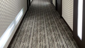 Corredor de hotel com paredes xadrez, carpete listrado e portas em ambos os lados.