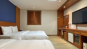 Quarto de hotel com duas camas, televisão, frigobar e um armário de madeira.