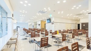 Uma cafeteria ampla com várias mesas e cadeiras, uma tela de televisão e um quadro branco na parede.