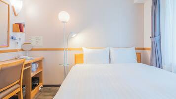 Quarto de hotel com uma cama, uma escrivaninha com cadeira, abajur e espelho.