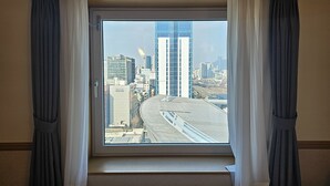 Quarto de hotel com uma grande janela que oferece vista para o horizonte urbano, incluindo edifícios altos e uma estrada.