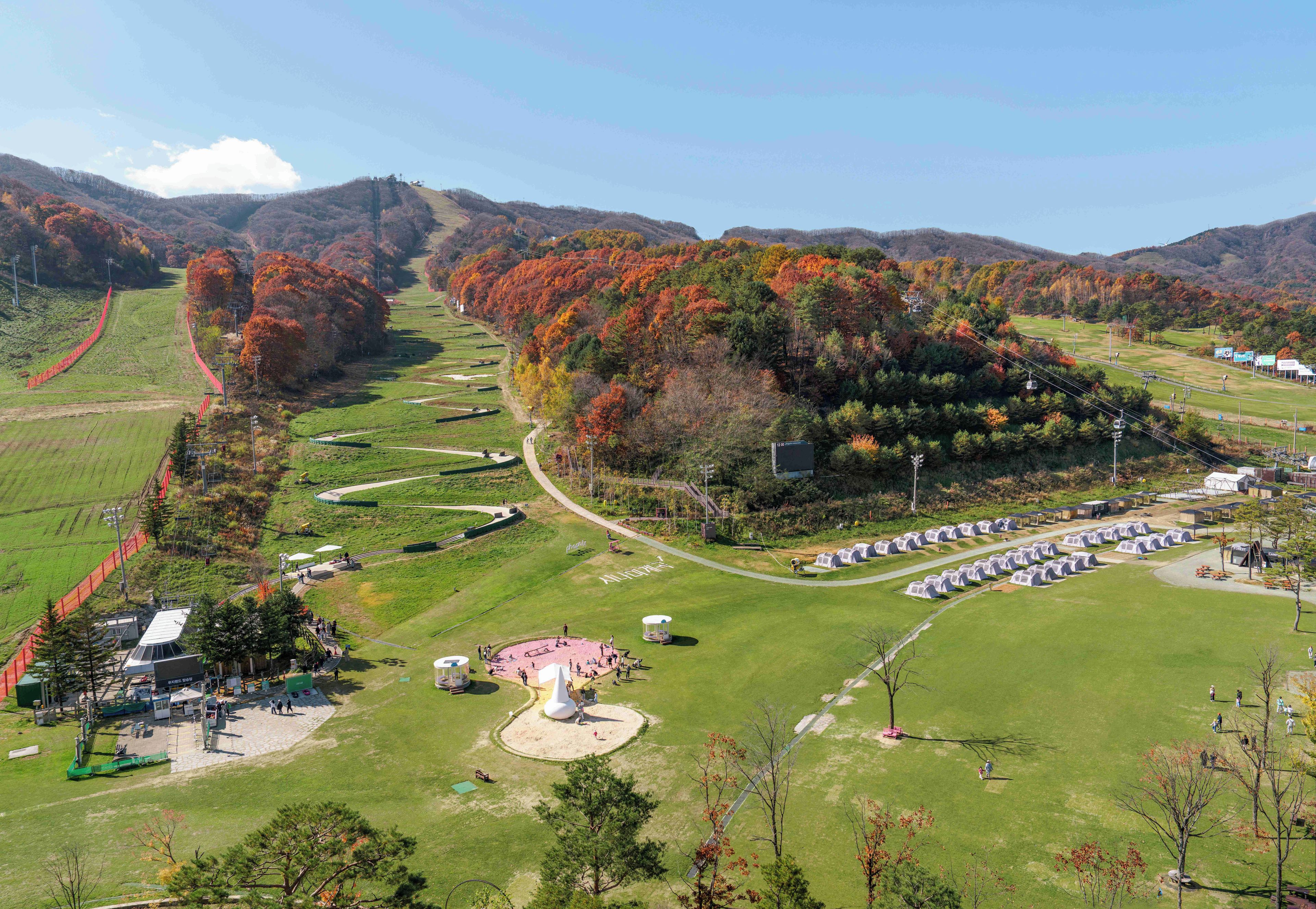 Um camping com tendas, área de piquenique e trilha para caminhada.