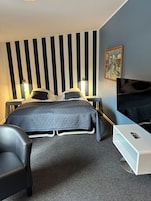 Quarto moderno com cama, mesas de cabeceira, televisão e um quadro na parede.