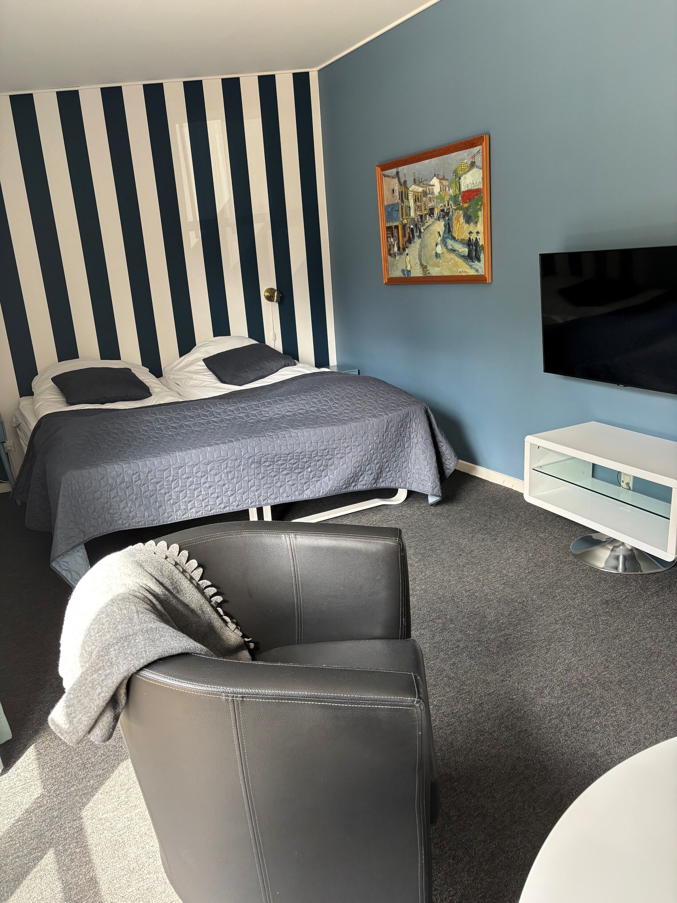 Quarto de hotel com uma cama, uma cadeira, uma televisão e um quadro na parede.