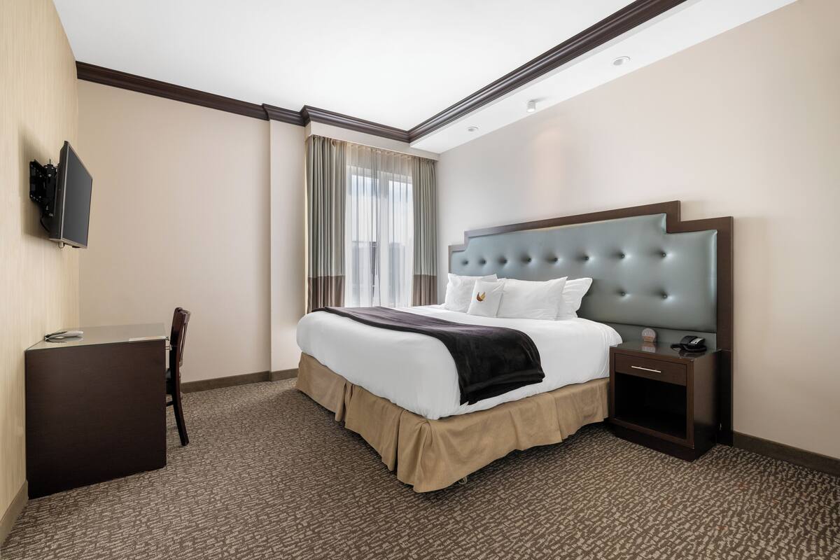 Quarto de hotel com uma cama grande, uma escrivaninha, uma cadeira e uma TV fixada na parede.