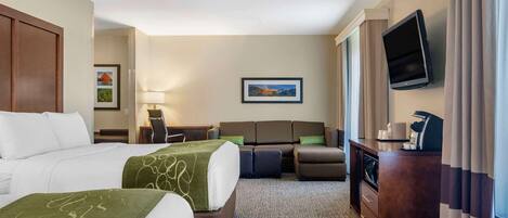 Quarto de hotel com duas camas, um sofá, uma escrivaninha com computador, televisão e janela com cortinas.