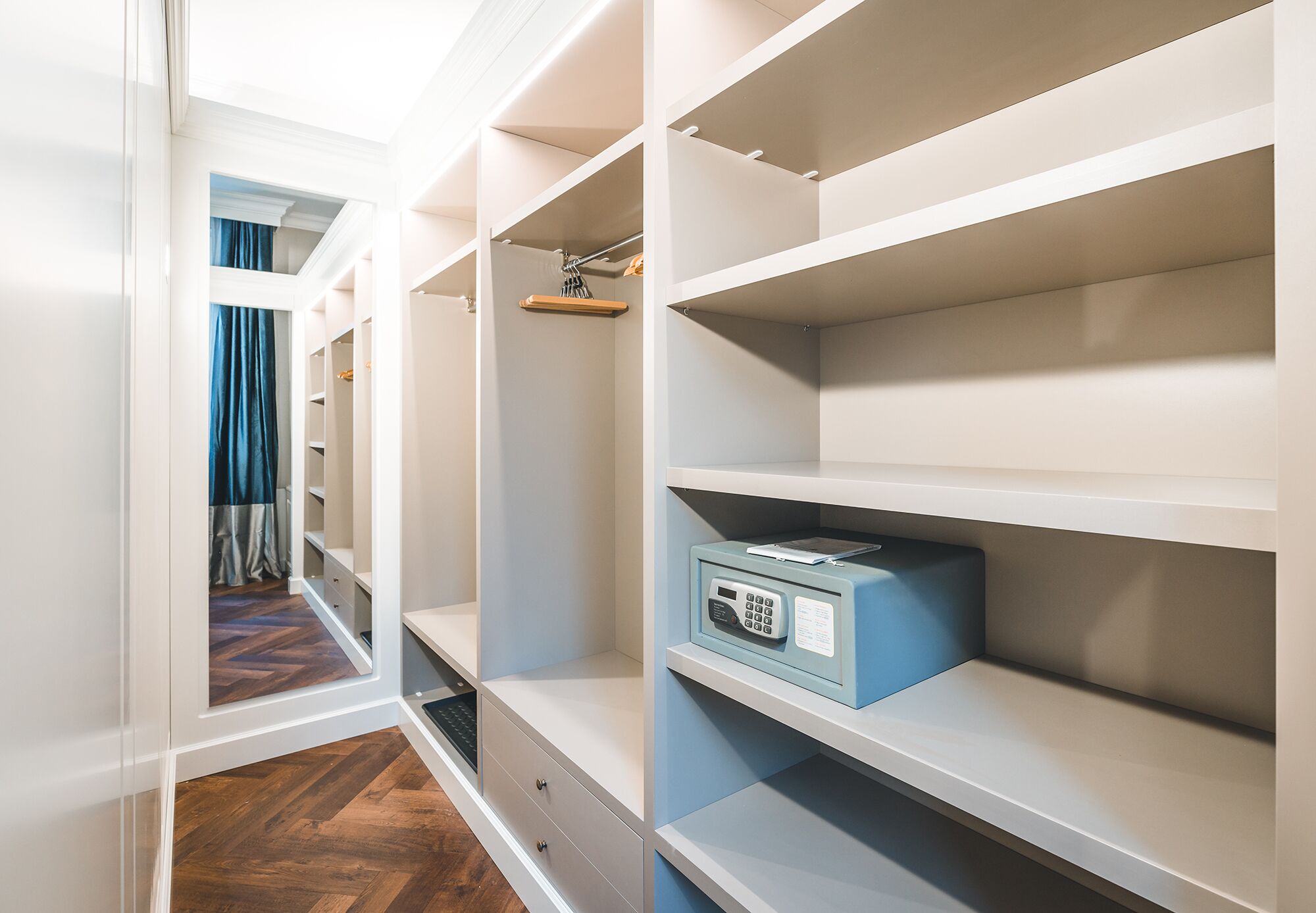 Um closet espaçoso com prateleiras abertas, uma barra para pendurar roupas e uma pequena caixa azul em uma das prateleiras.