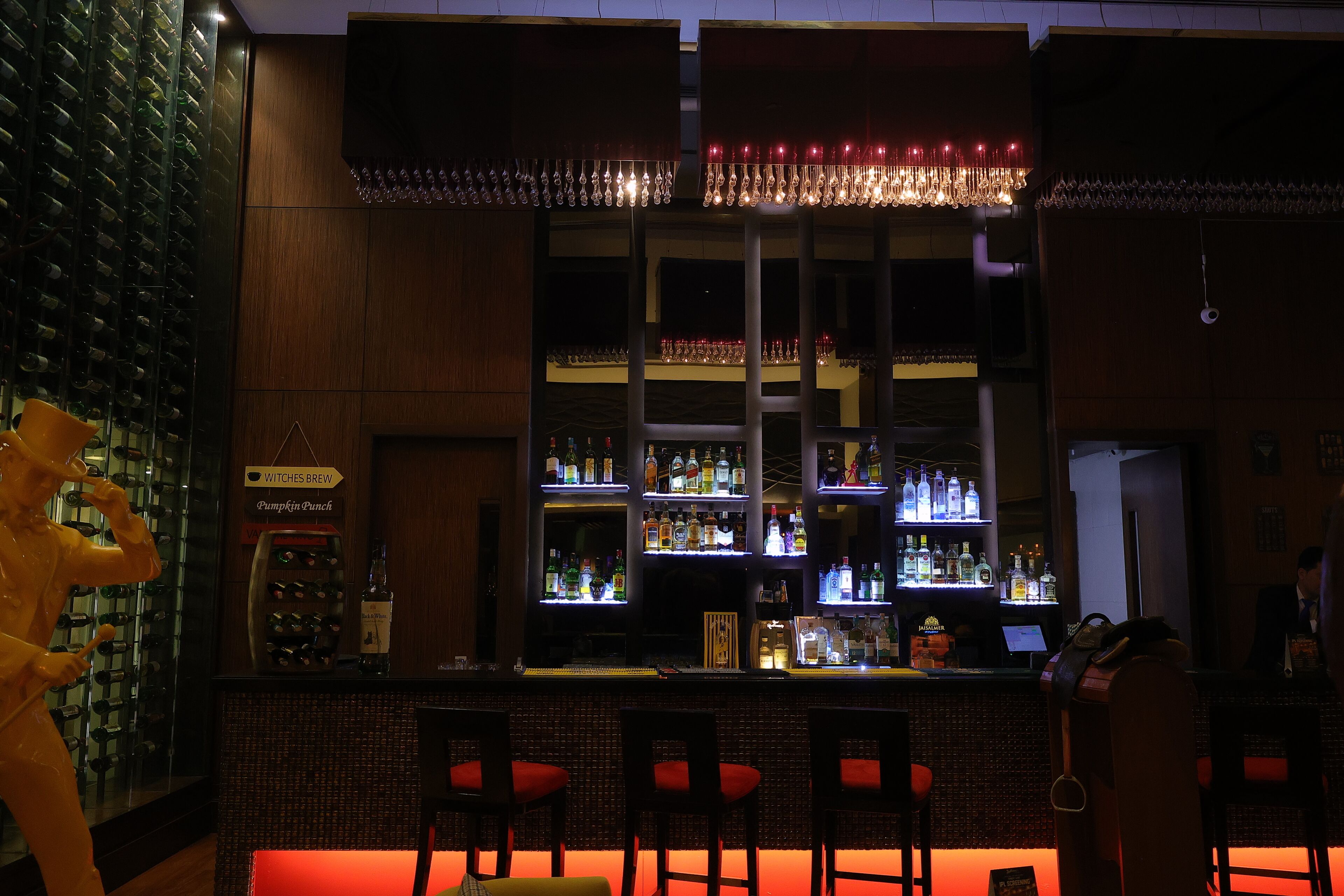 Uma área de bar com adega, banquetas e um bartender.