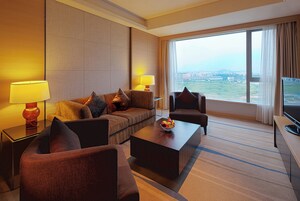 Quarto de hotel com sofá, poltronas, mesa de centro e televisão.