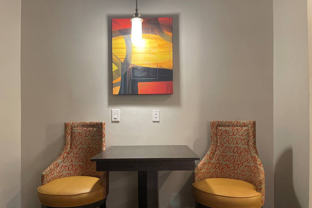 Duas cadeiras com estampa e almofadas amarelas, uma mesa e um quadro pendurado na parede acima.