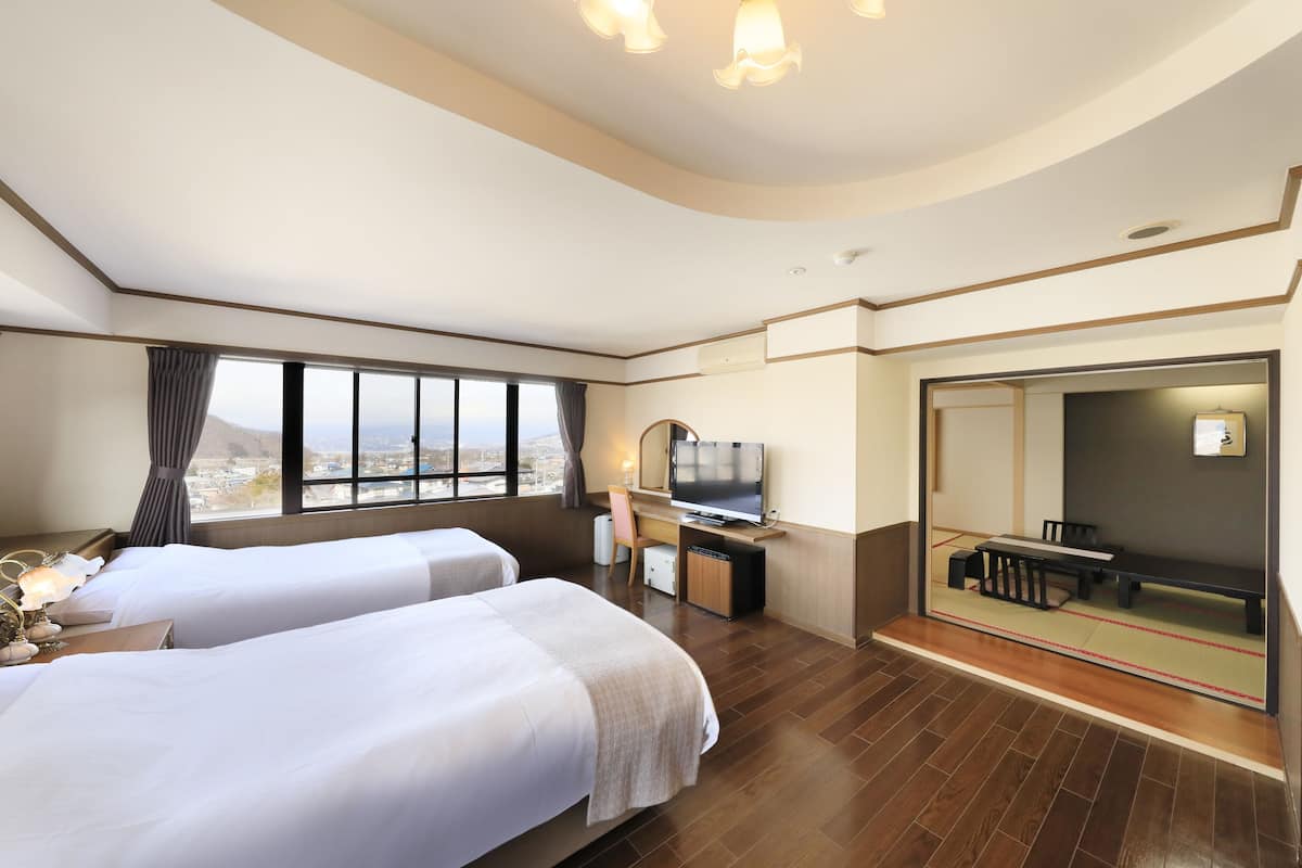 Quarto de hotel com duas camas, televisão, escrivaninha, cadeira, espelho e vista para a cidade.