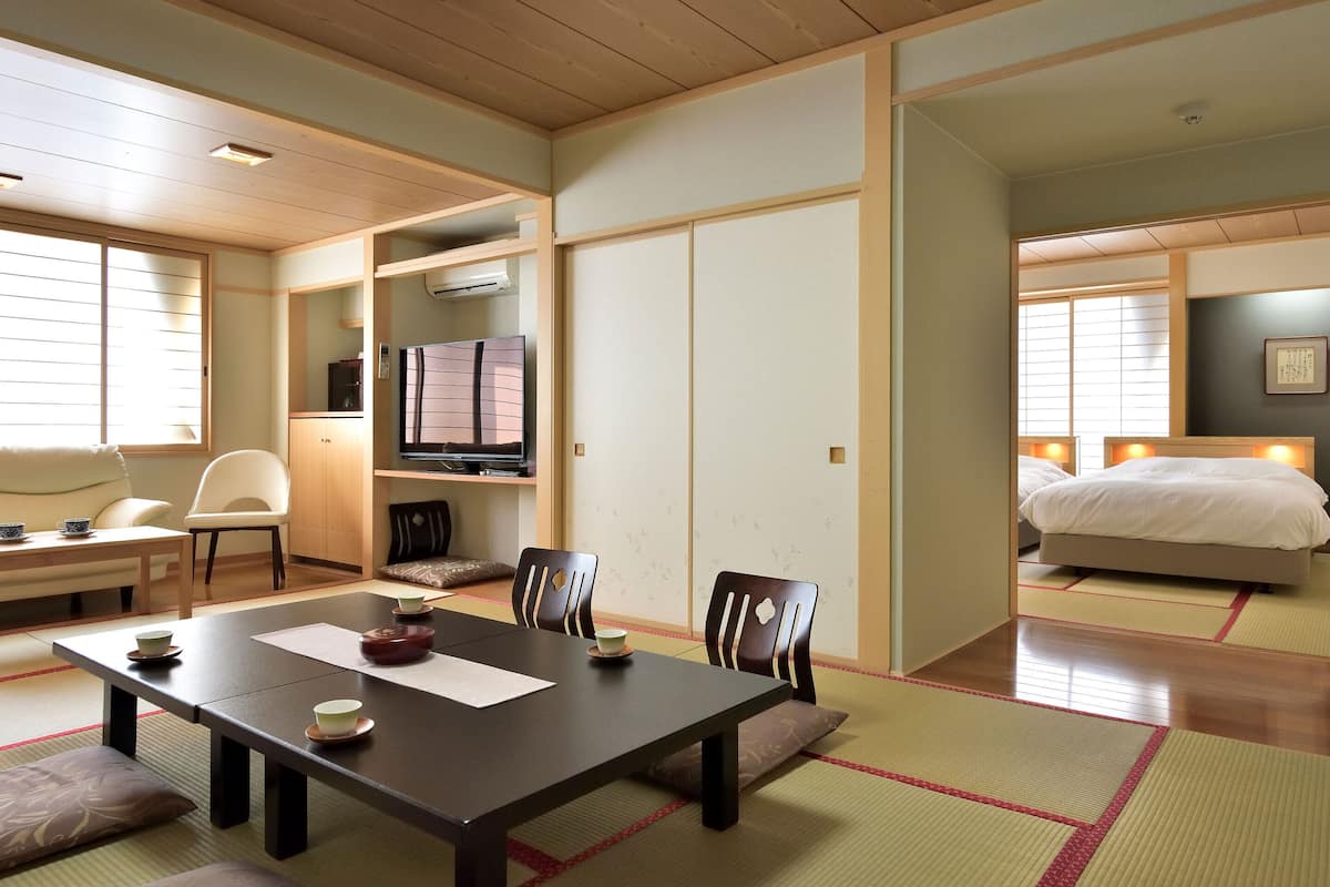 Quarto tradicional japonês com tatames, uma mesa baixa com almofadas, uma televisão e uma cama com futon.