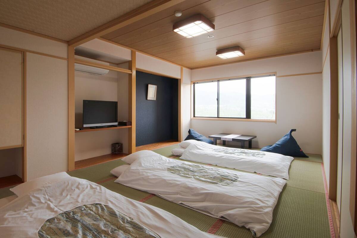 Quarto em estilo japonês tradicional com tatames, duas camas, uma televisão e uma porta deslizante.
