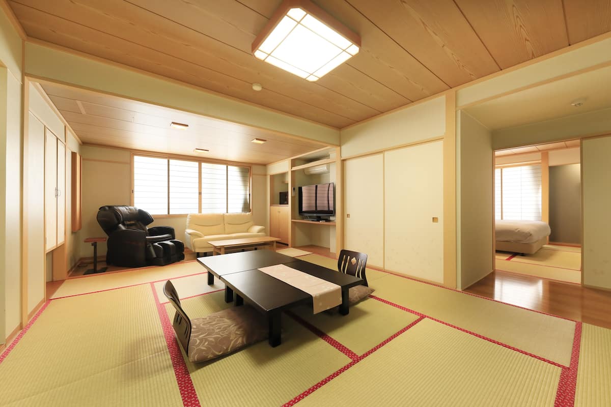 Quarto em estilo japonês tradicional, com piso de tatame, mesa baixa, sofá e televisão.
