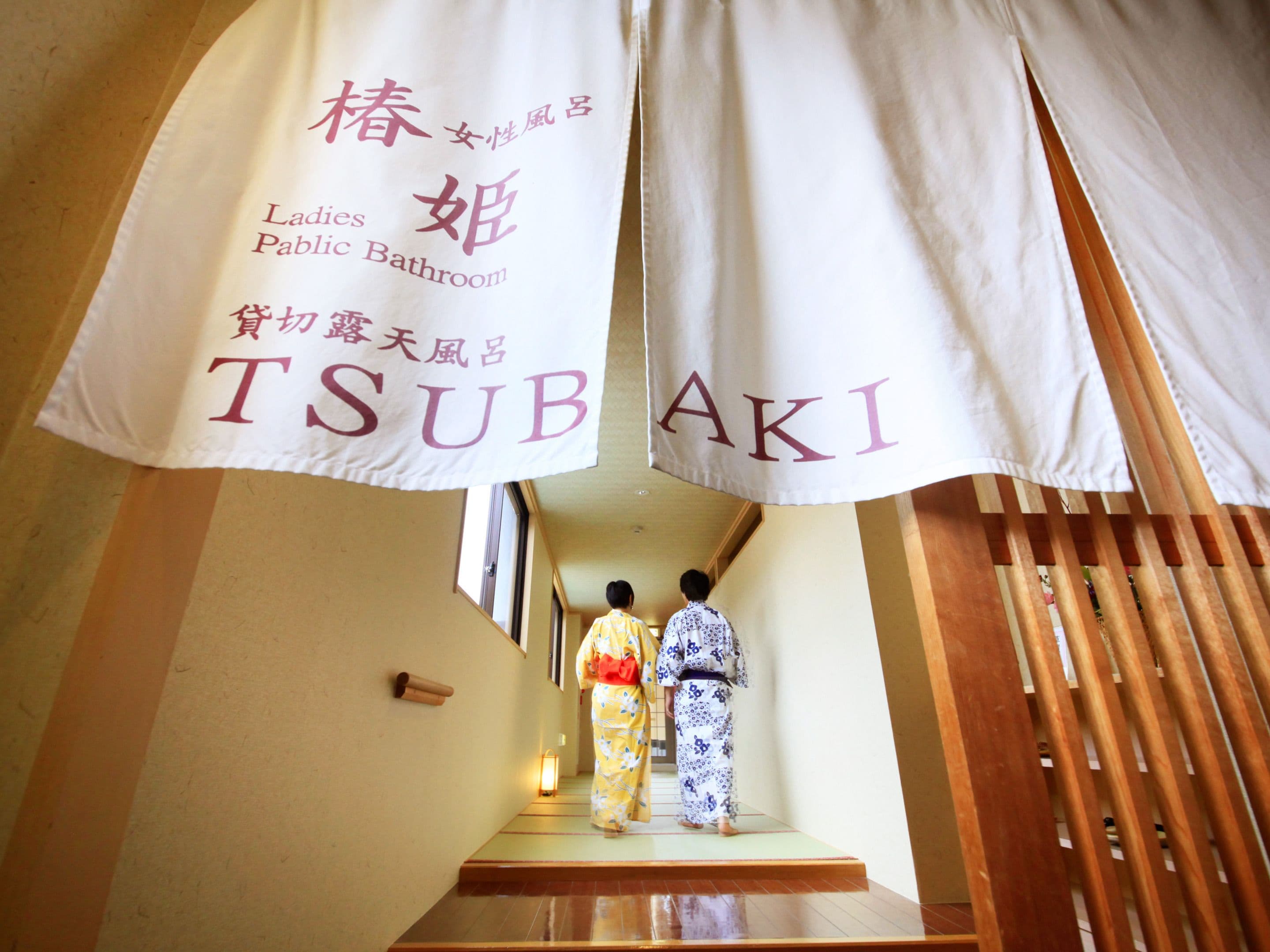 Interior tradicional japonês com escada de madeira e duas pessoas vestidas com quimonos.