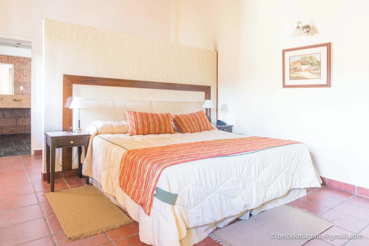 Uma cama bem arrumada com um cobertor listrado, uma cabeceira de madeira e uma pequena mesa de cabeceira com uma luminária.