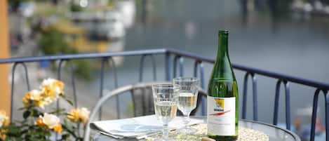 Uma mesa com uma garrafa de vinho, duas taças e uma rolha, sobre uma mesa redonda com vista para um lago e barcos ao fundo.