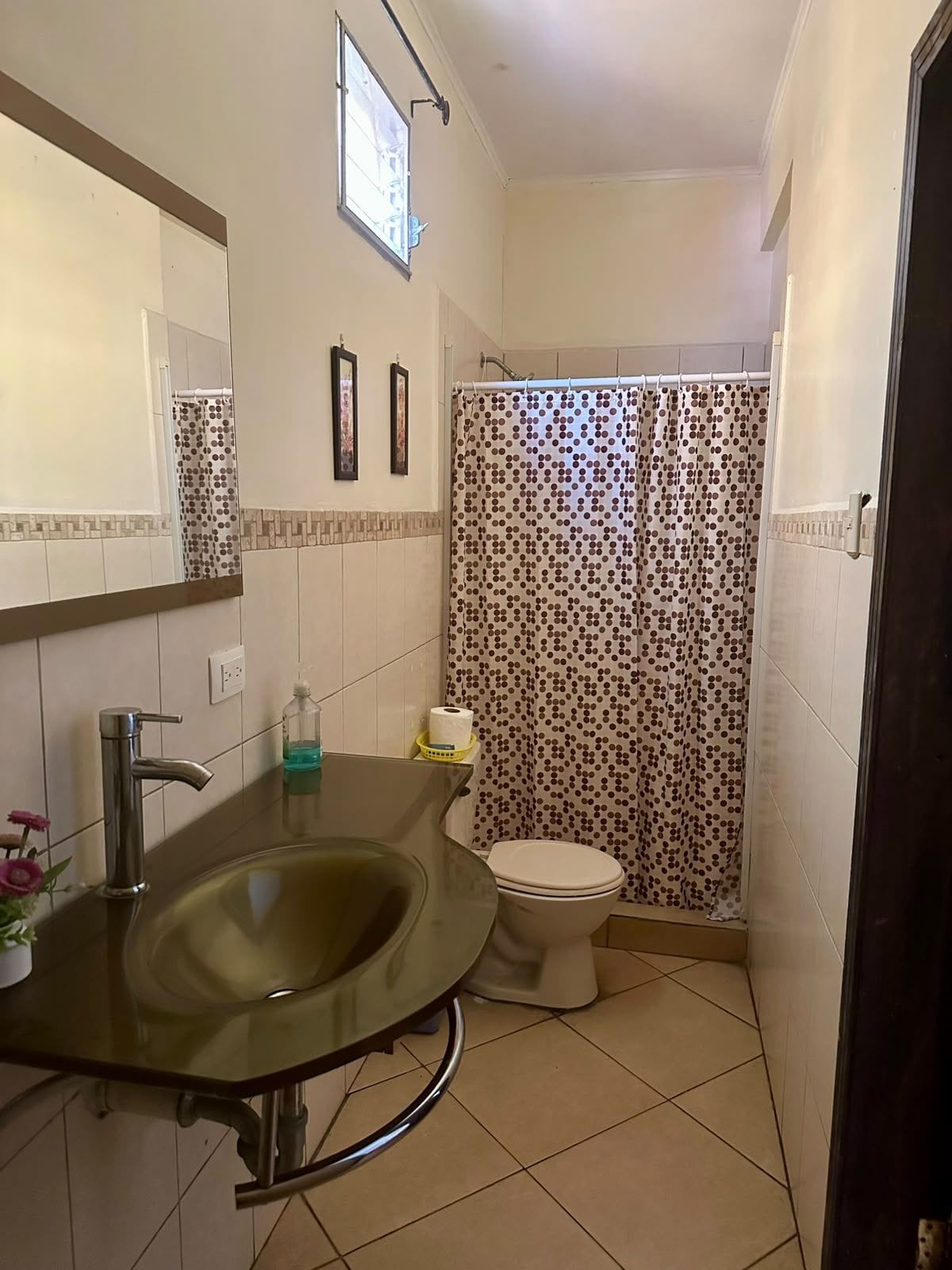 Casa de banho com lavatório de vidro, sanita e cortina de chuveiro com padrão de bolinhas.