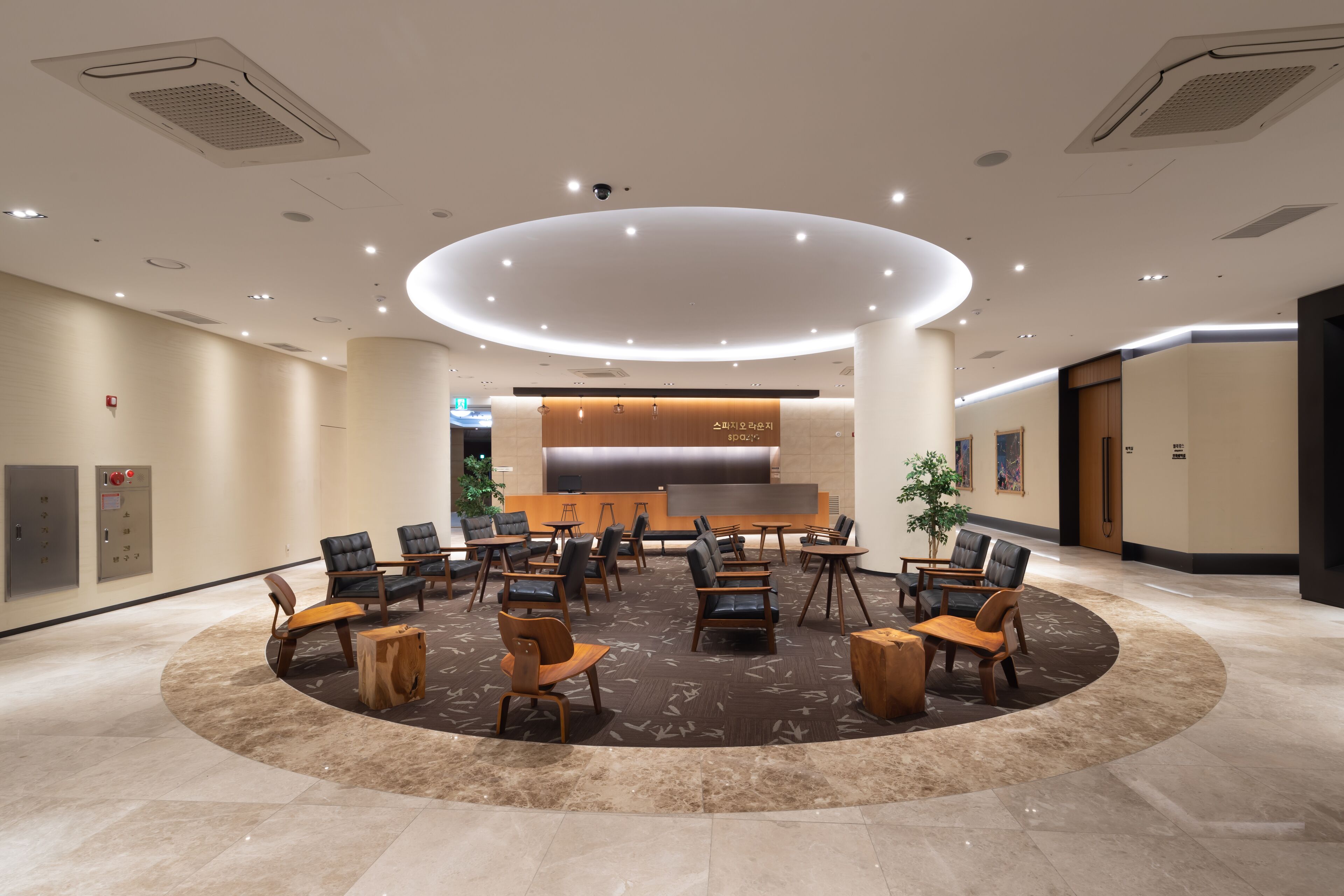 Um hall amplo com uma receção central, diversas áreas de estar e um design moderno no teto.