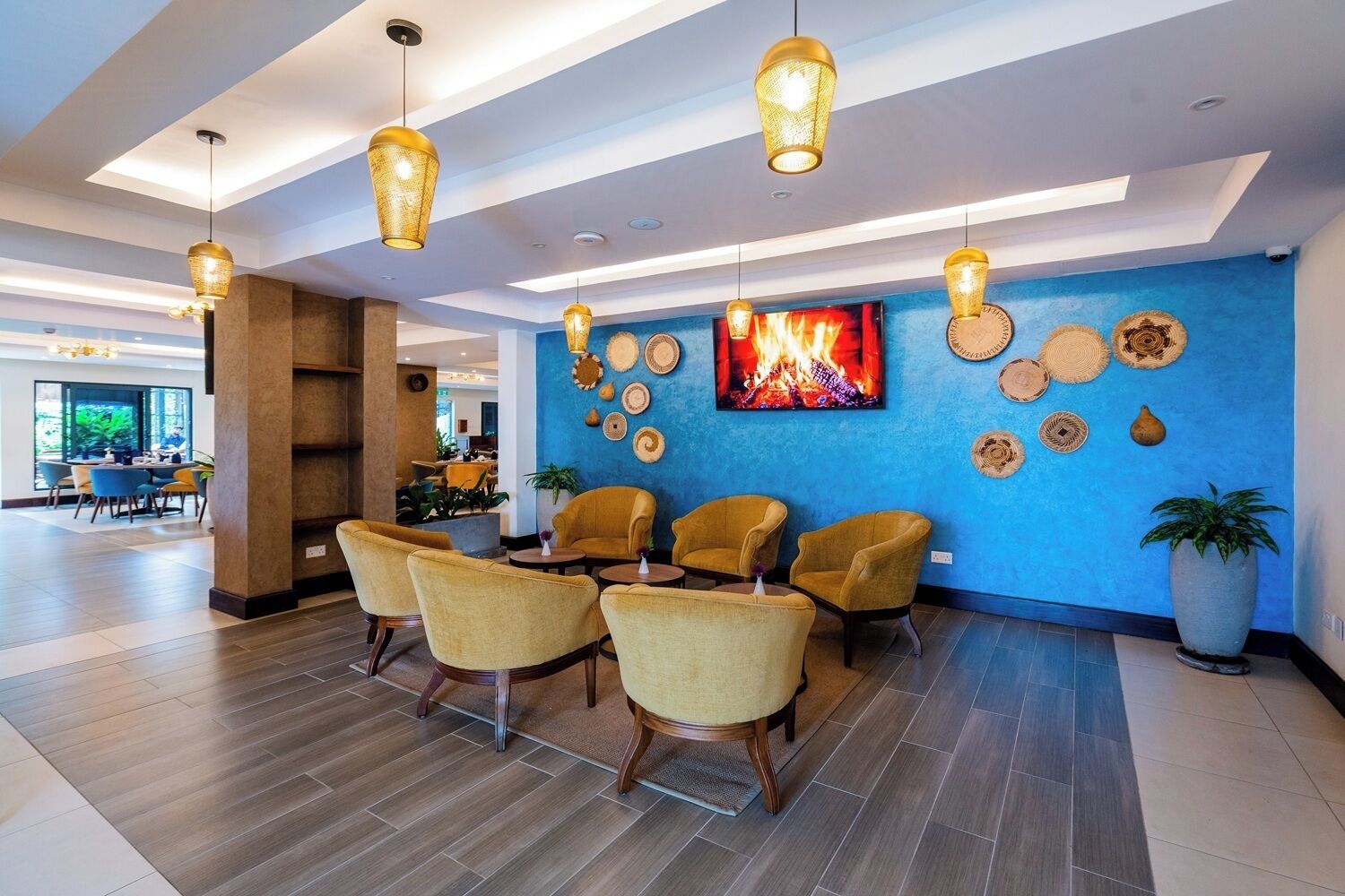 Um lobby moderno com parede azul de destaque, lareira e área de estar com cadeiras amarelas.