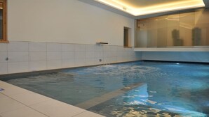 Piscina interior com água cristalina, paredes azulejadas e teto com iluminação embutida.