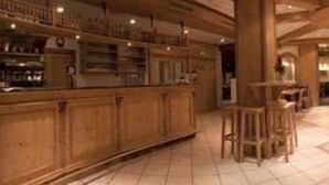 Um quarto espaçoso com um bar de madeira, uma mesa de jantar e um lustre grande.