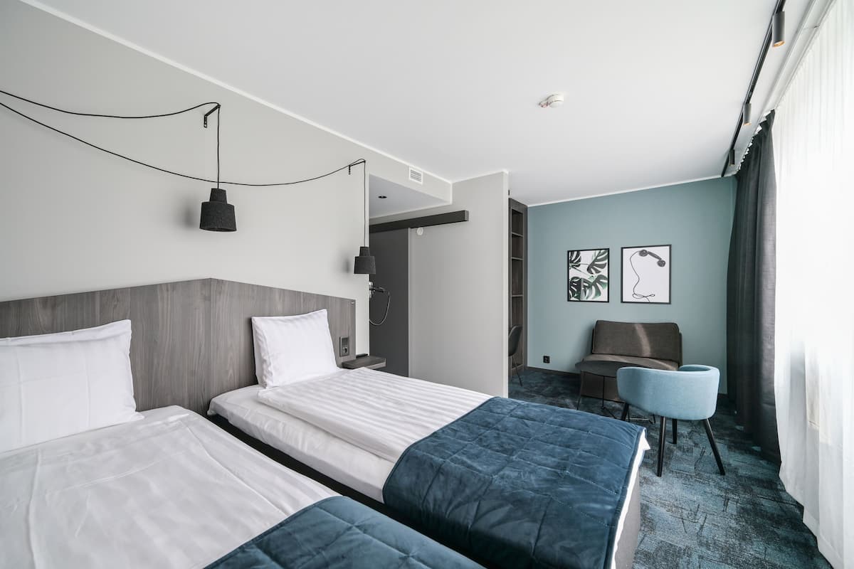 Quarto de hotel com duas camas, uma escrivaninha, uma cadeira e obras de arte na parede.