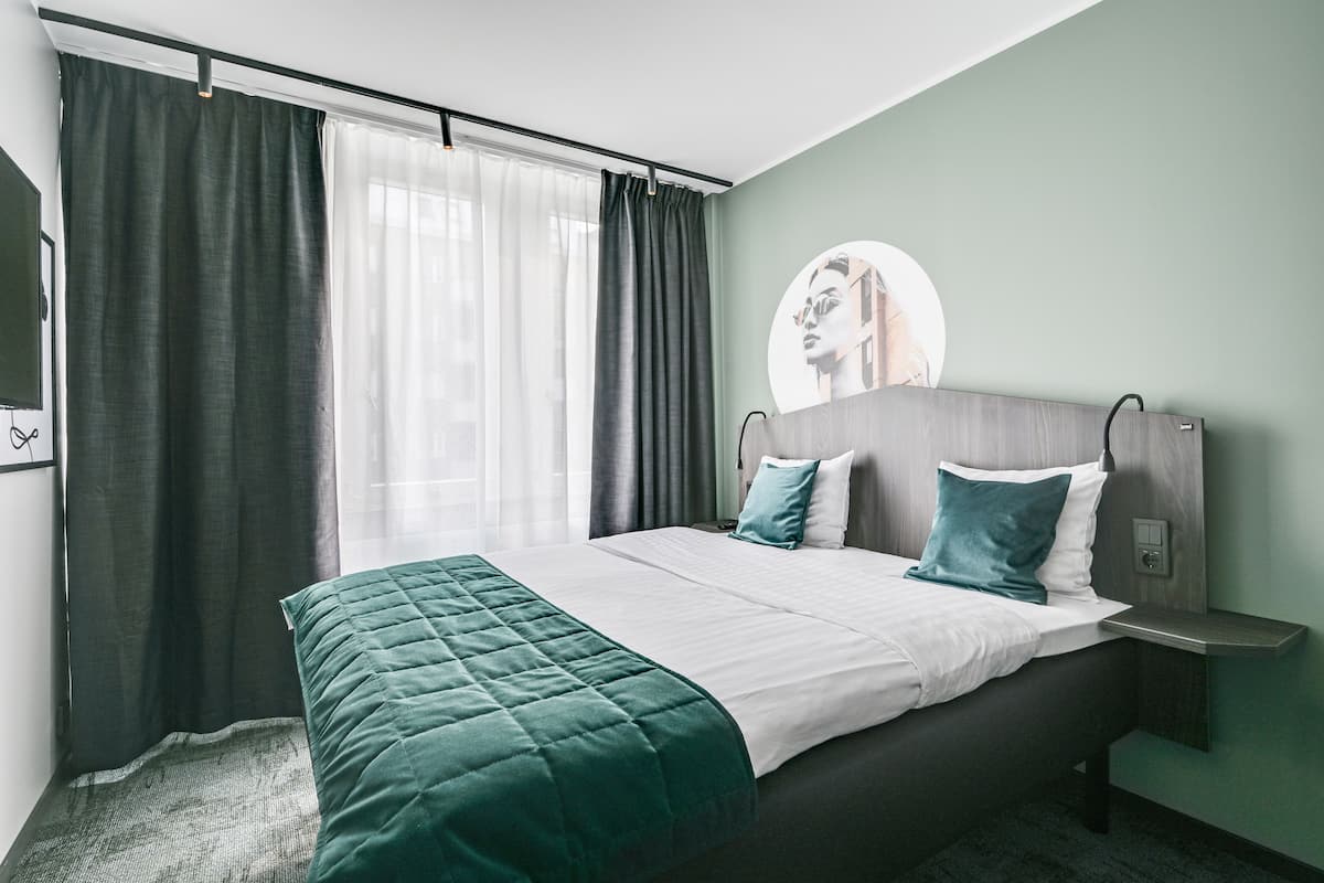 Quarto de hotel moderno com uma cama grande, cortinas escuras, um ornamento redondo na parede e uma mesinha de cabeceira.