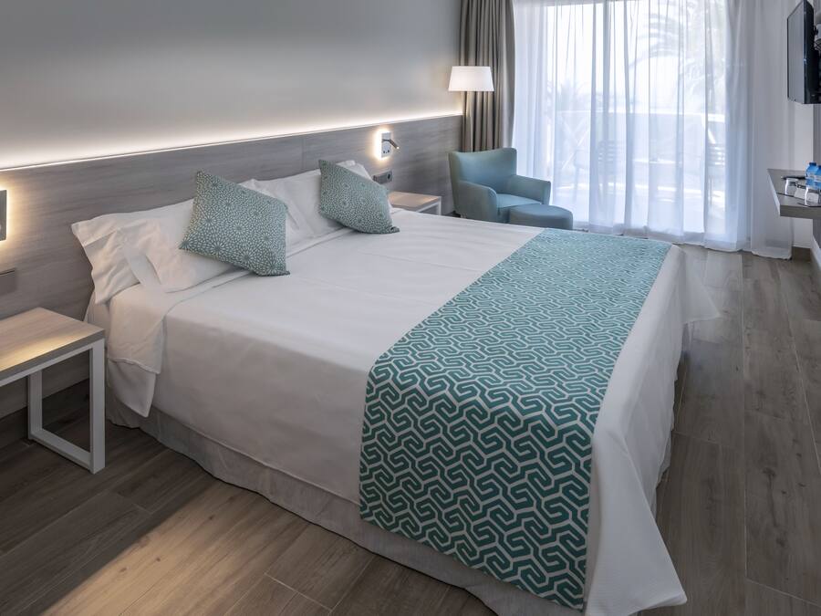 Quarto de hotel moderno com uma cama grande, mesas de cabeceira, um espaço para sentar e uma televisão.