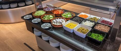 Buffet com diversos alimentos, incluindo saladas, frutas e proteínas.