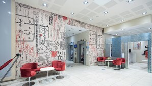 Um hall moderno com assentos vermelhos, piso branco e paredes cobertas por diversas escritas e desenhos.