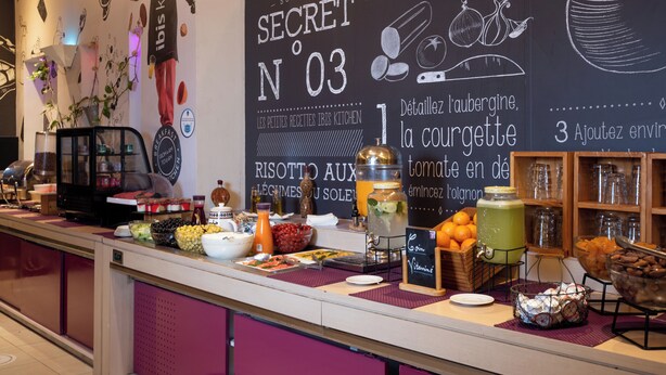 Espaço do buffet de café da manhã com cardápio em lousa, diversas opções de alimentos e máquina de café.