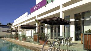 Piscina com deck de madeira e grades de metal, área de estar externa com guarda-sóis e um edifício com a placa 'WOK Restaurant'.