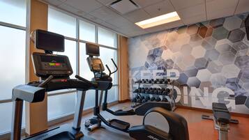 Uma academia com equipamentos de cardio, halteres e uma parede com frases motivacionais.