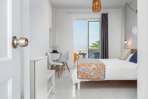 Quarto de hotel moderno com cama, escrivaninha e cadeira, varanda com vista e luminária pendente.