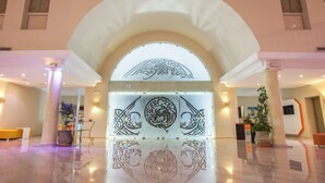 Um hall amplo com teto alto, um arco decorativo central e um balcão de recepção.