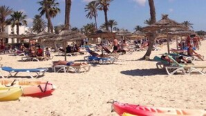 Uma praia com palmeiras, espreguiçadeiras e guarda-sóis.