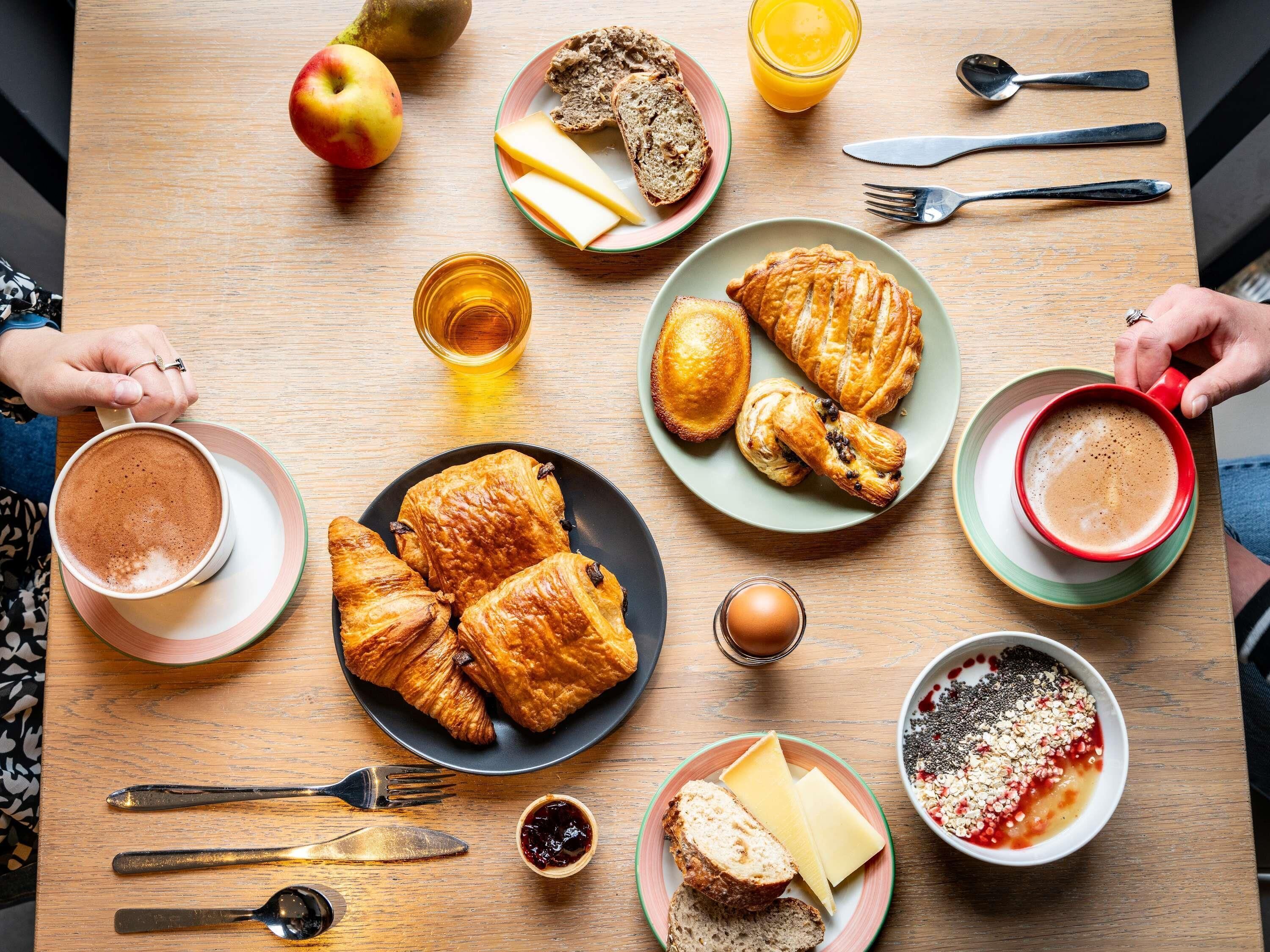 Uma mesa de café da manhã com croissants, queijo, pão e uma tigela de cereal.