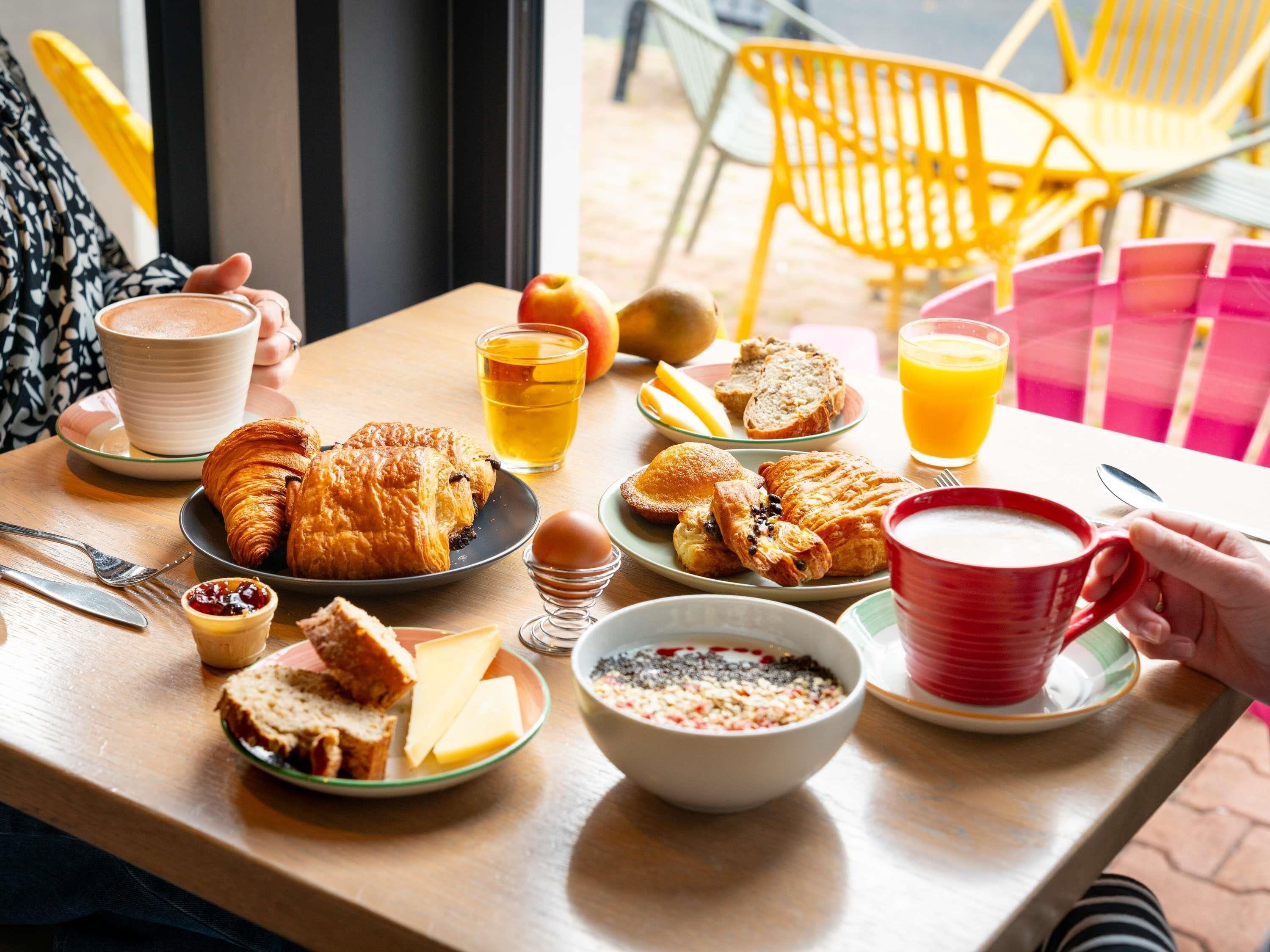Mesa de café da manhã com croissants, pão, ovos e bebidas.