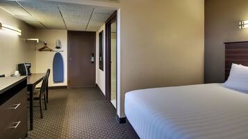 Quarto de hotel com uma cama, uma escrivaninha com cadeira, um cabideiro e uma porta que dá para outro cômodo.