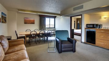 Quarto de hotel com área de jantar, cozinha compacta, sofá de couro marrom, poltrona azul e pequena mesa.