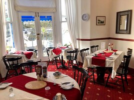 Interior de restaurante com mesas redondas, cadeiras pretas e toalhas de mesa vermelhas.