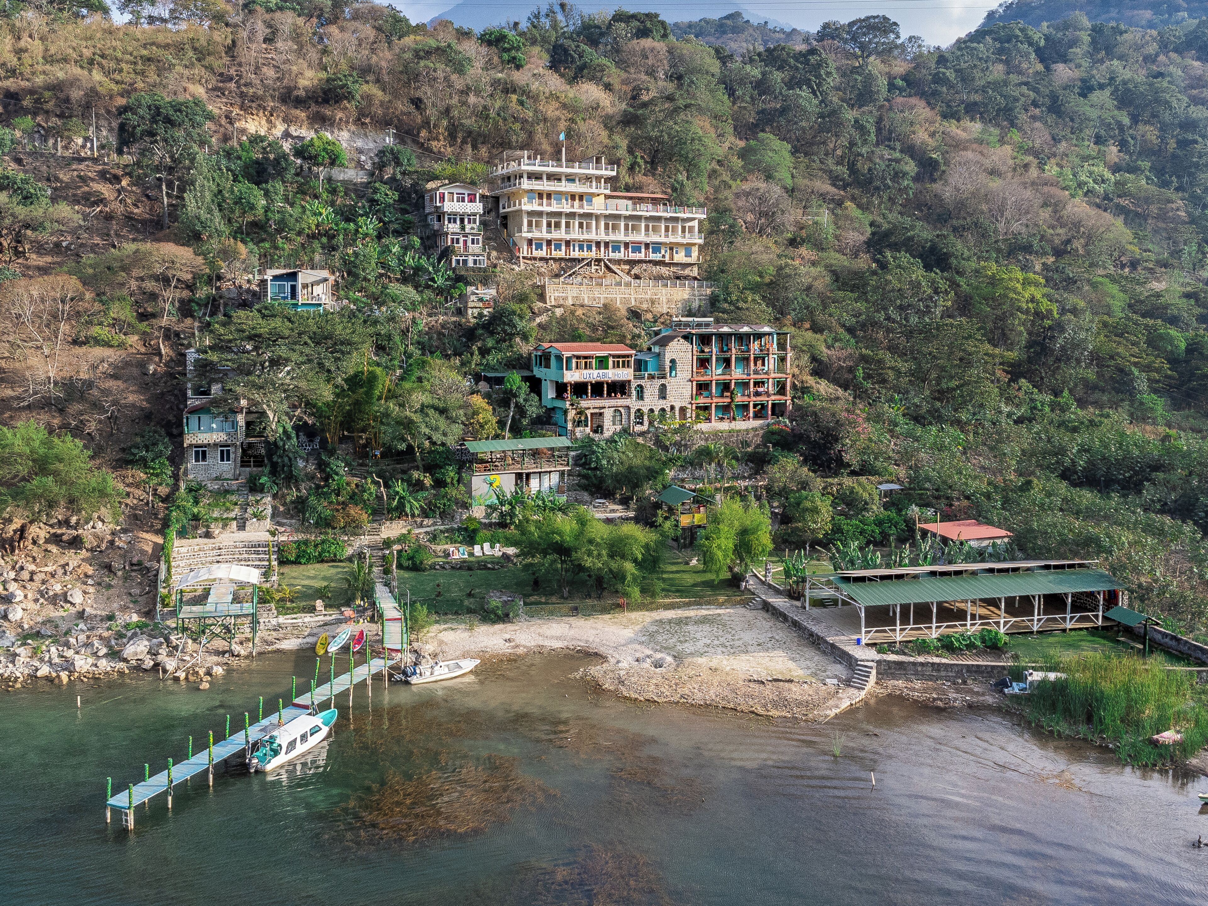 Hotel de vários andares com vista para um rio, um cais com barco e vegetação ao redor.