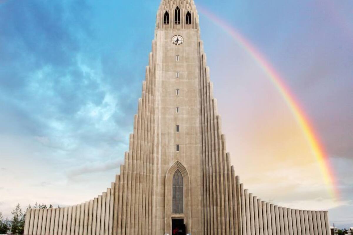 Um edifício grande e simétrico, com telhado pontiagudo e um relógio na fachada.